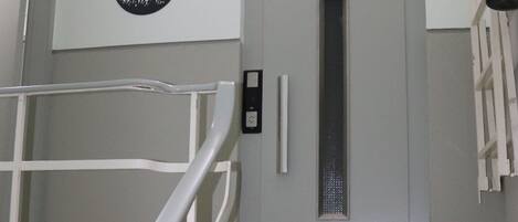 Uma escadaria com grades brancas que leva a uma porta, onde um extintor de incêndio está fixado na parede.
