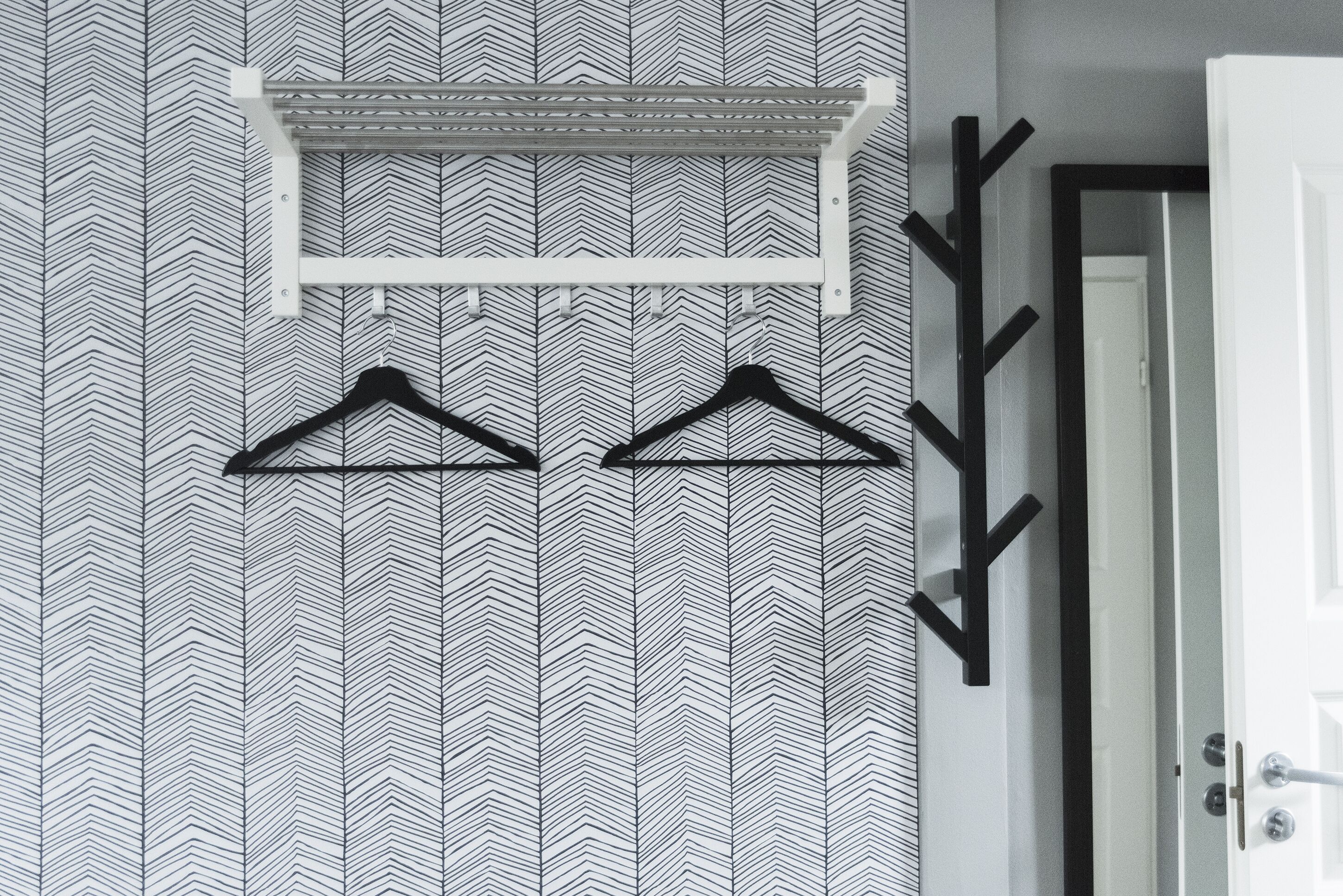 Um banheiro com papel de parede estampado, um porta-toalhas branco e um gancho preto.