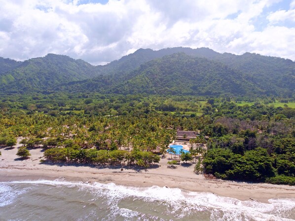 Uma praia com piscina e palmeiras, rodeada por colinas verdes e exuberantes.