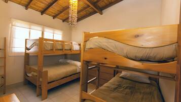 Quarto com duas beliches, mobiliário de madeira, um candelabro e uma janela com persianas.