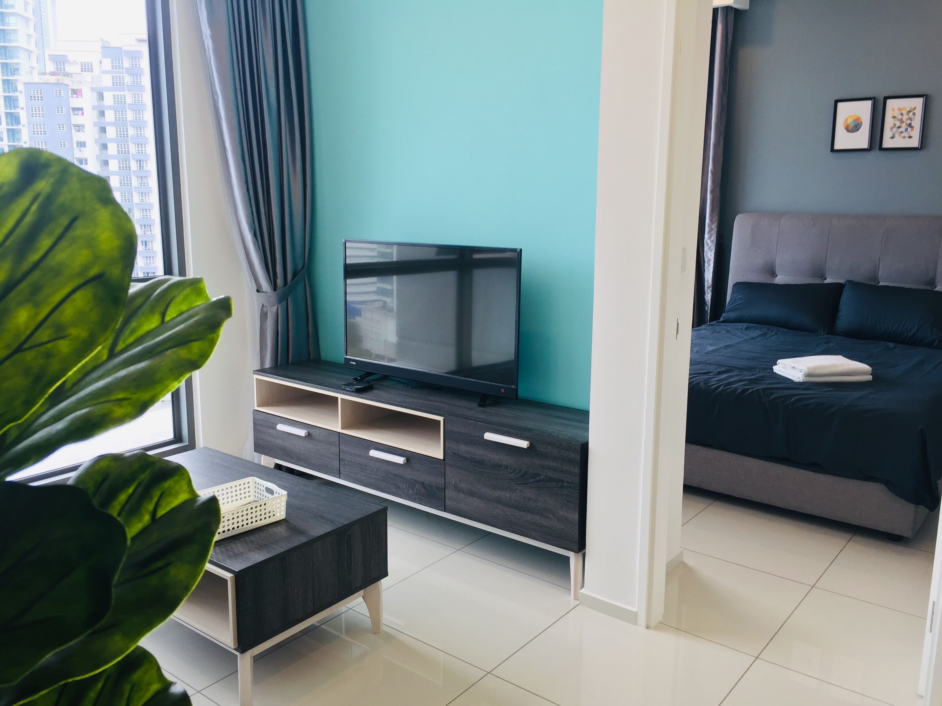 Quarto de hotel moderno com televisão de tela plana sobre um aparador de madeira escura, cama com roupa de cama escura e uma janela grande com cortinas.