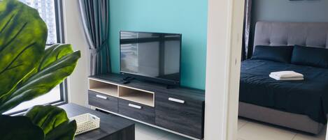 Quarto de hotel moderno com televisão de tela plana sobre um aparador de madeira escura, cama com roupa de cama escura e uma janela grande com cortinas.
