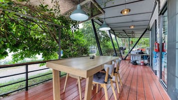Um deck de madeira com mesa e cadeiras, rodeado por vegetação e uma área coberta com luzes penduradas.