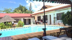 Área de piscina com espreguiçadeiras e um alpendre coberto.