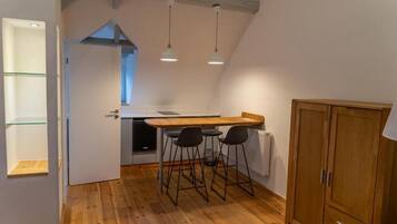 Uma cozinha compacta com mesa de madeira, banquetas de bar, armário de madeira e iluminação pendente.