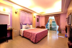 Um quarto com cama, escrivaninha, cadeira, televisão e varanda com cortinas.