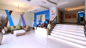 Um hall moderno com balcão de atendimento, área de estar, escada e parede decorativa.