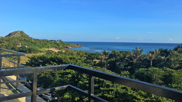 Uma varanda com vista para uma paisagem costeira, incluindo uma montanha, praia e oceano.