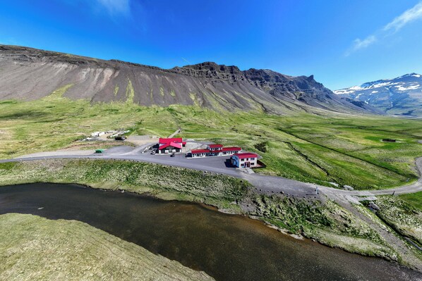 Localização remota e pitoresca com um pequeno conjunto de edifícios com telhados vermelhos, estrada pavimentada e paisagem natural ao fundo com montanhas.