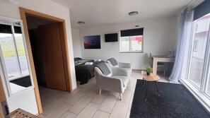 Quarto de hotel com uma cama, duas poltronas, uma mesinha com uma planta, televisão e janela com vista para o exterior.