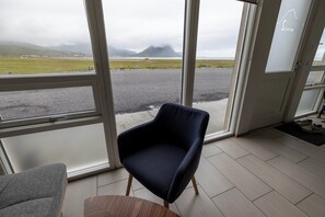 Quarto com uma grande janela que oferece vista para um campo gramado e montanhas.