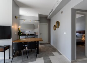 Cozinha moderna com área de jantar, televisão e quarto visível por uma porta aberta.