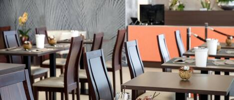 Um restaurante com mesas e cadeiras de madeira, uma parede de pedra e uma televisão ao fundo.