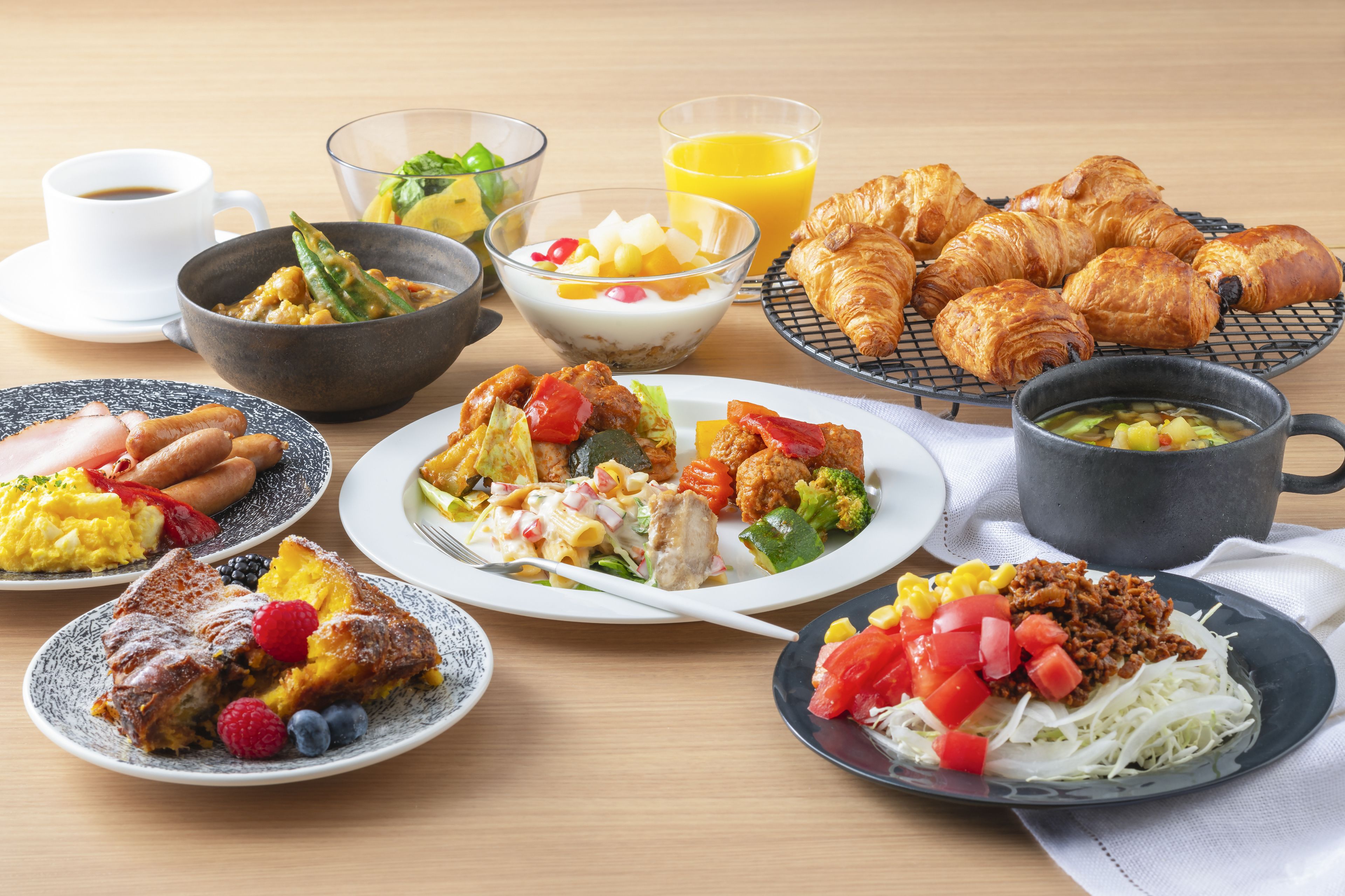 Uma mesa de café da manhã com diversos pratos, incluindo croissants, ovos mexidos e uma tigela de frutas.