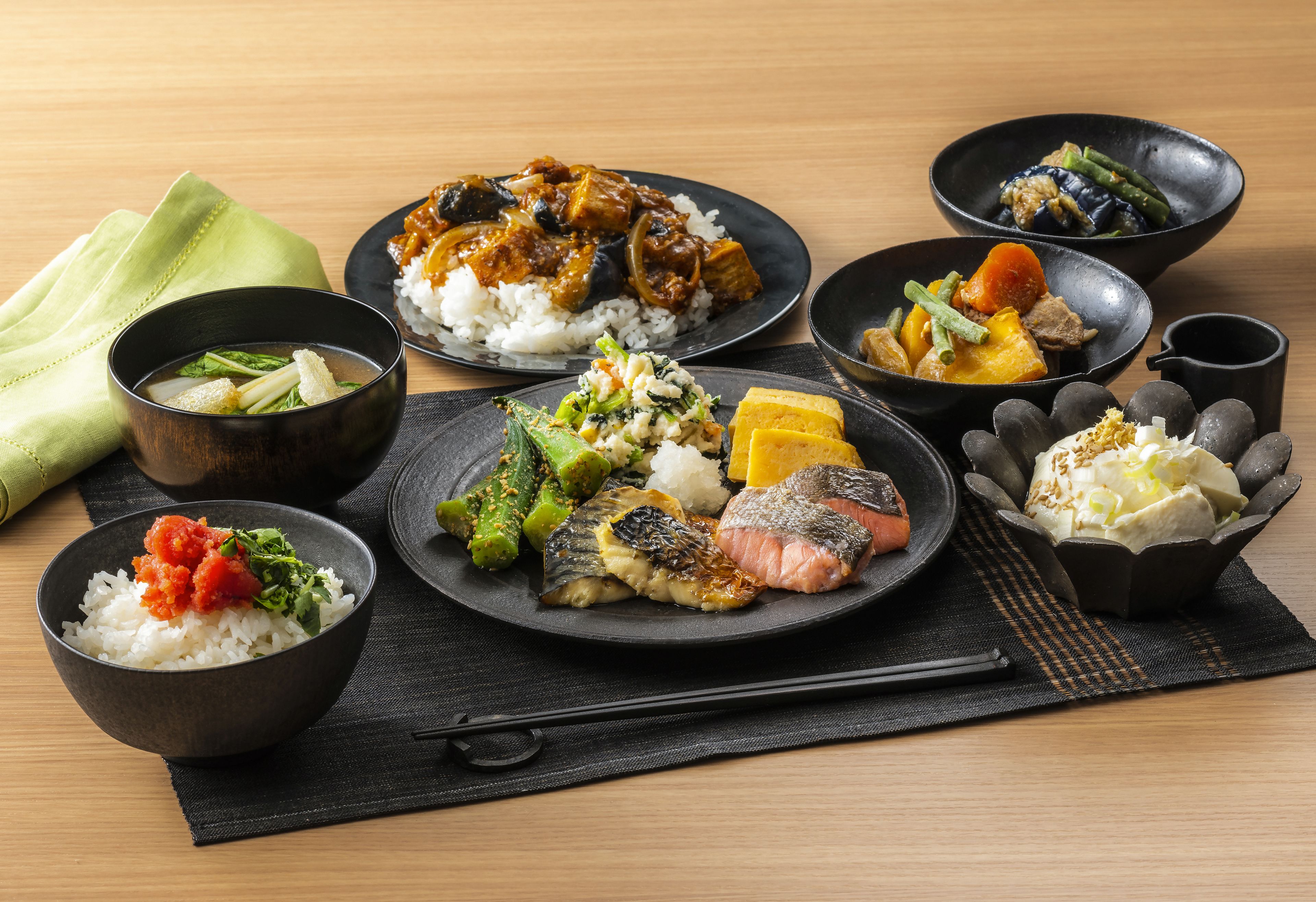 Diversos pratos japoneses, incluindo arroz, peixe e legumes, servidos em pratos pretos com hashis e uma tigela de sopa.