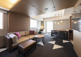 Quarto de hotel moderno com sofá, mesa redonda, espaço de refeições e um espelho grande.