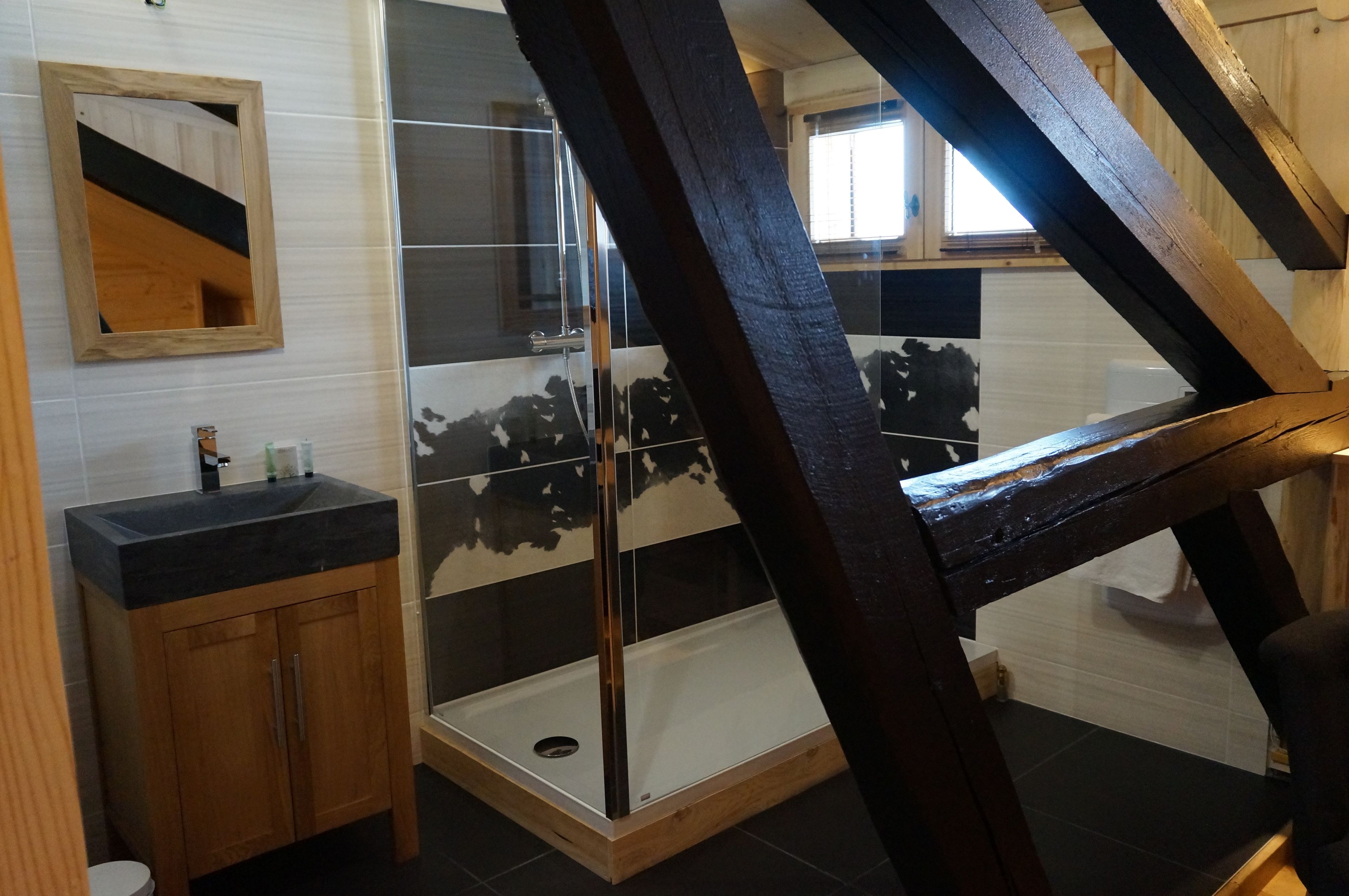 Casa de banho com armário de madeira, lavatório preto e cabine de duche em vidro.