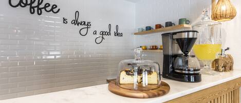 Uma bancada de cozinha com uma cafeteira, um recipiente de vidro com líquido amarelo e uma estatueta de elefante decorativa.