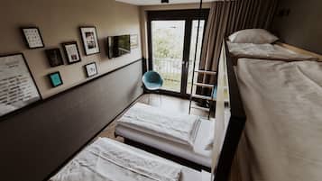 Quarto de hotel compacto com duas camas, um pequeno espaço de estar e uma janela com vista.