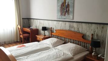 Quarto de hotel com cama de madeira, escrivaninha com cadeira, luminária e pintura na parede.