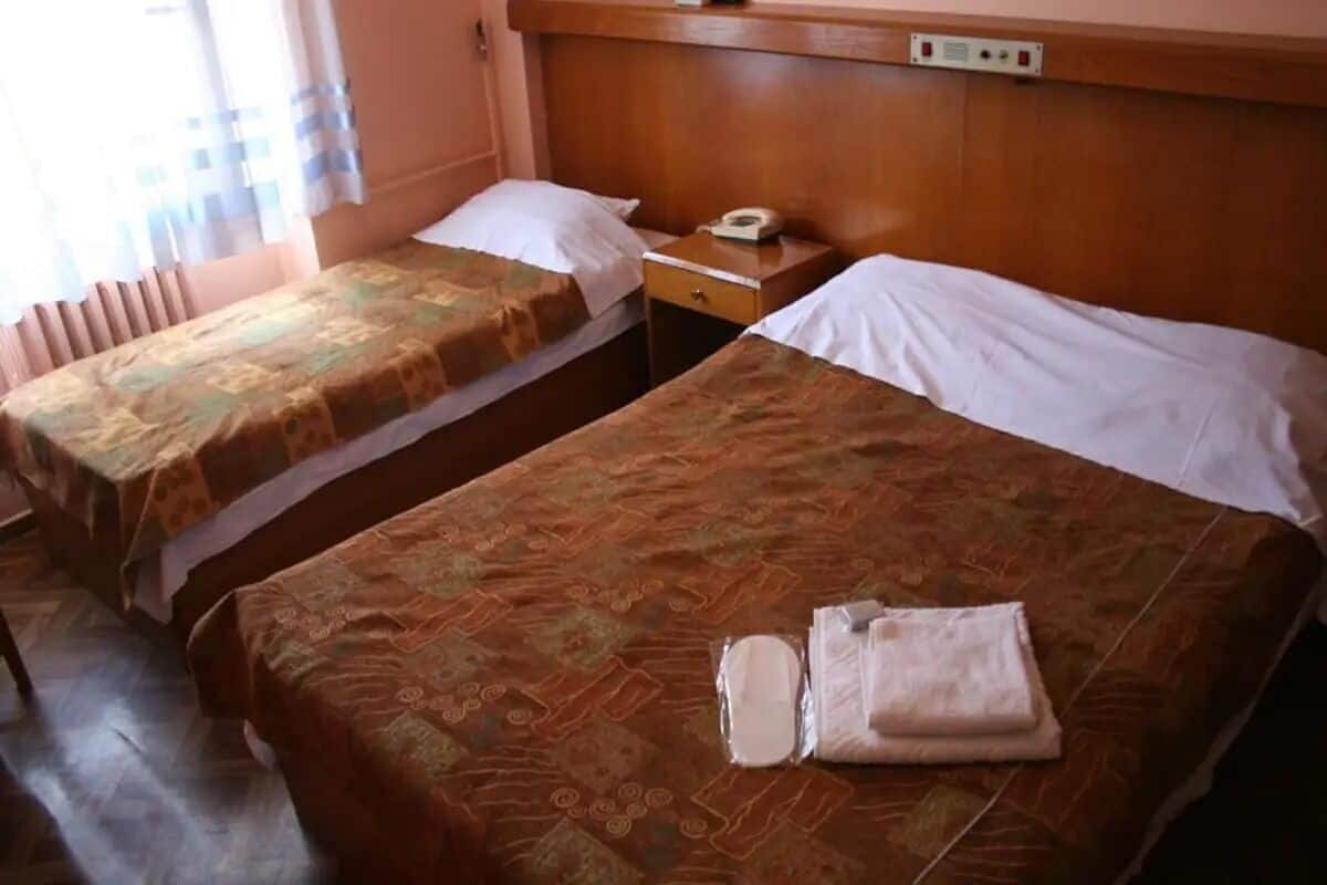 Quarto de hotel com duas camas, uma mesa de cabeceira com telefone e uma tomada na parede.