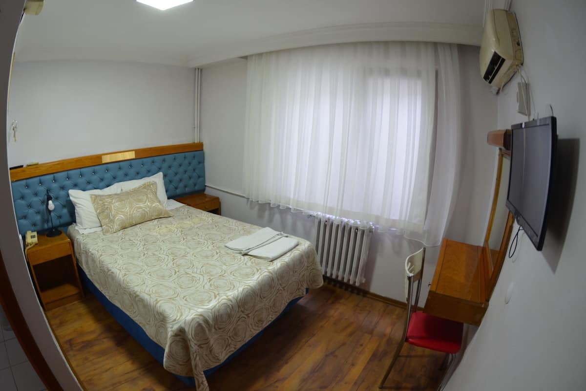 Quarto de hotel com cama, mesa de cabeceira, abajur e televisão.