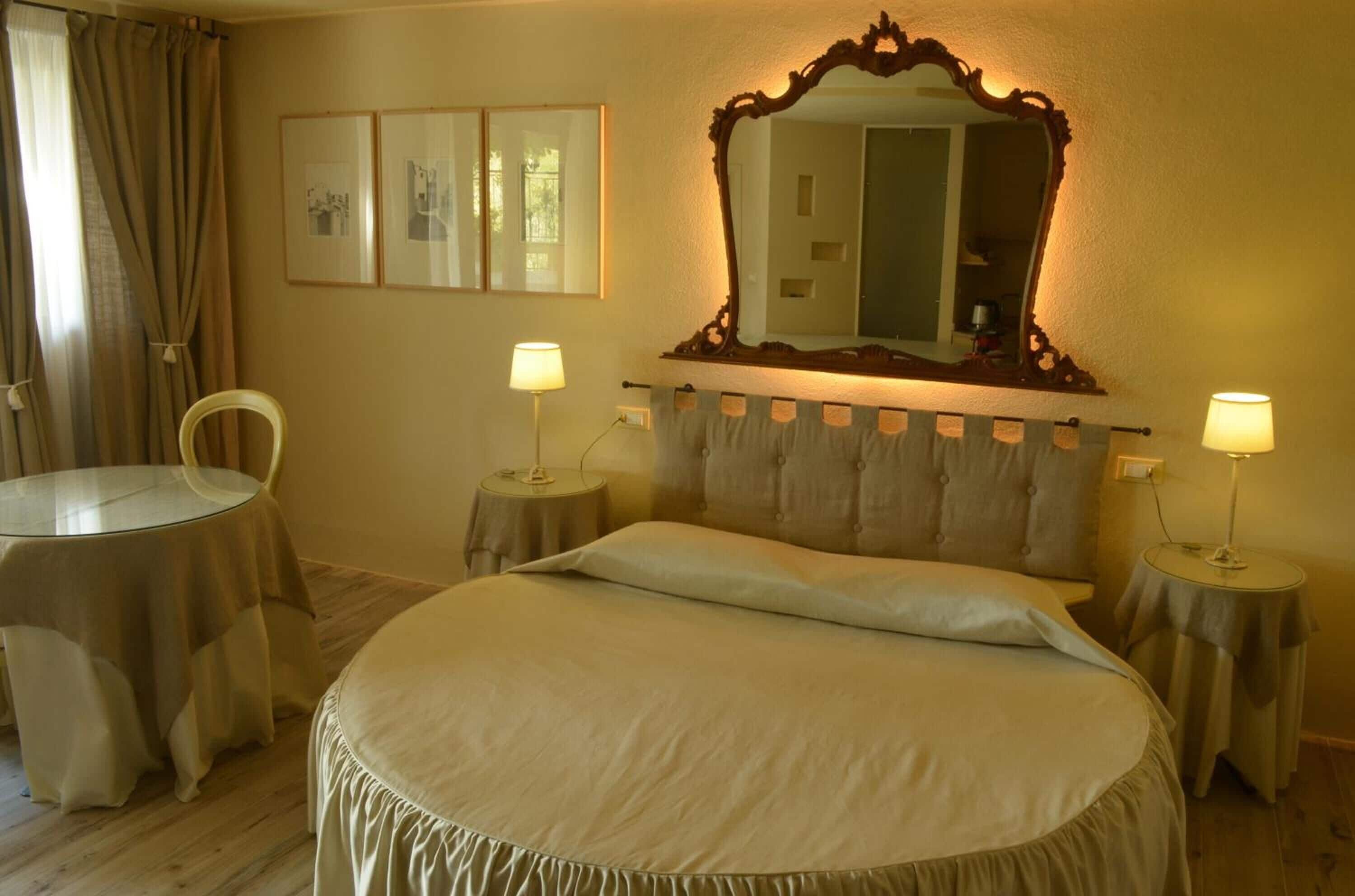 Quarto bem arrumado com uma cama grande, duas mesas de cabeceira com abajures, uma mesa redonda e uma cadeira.