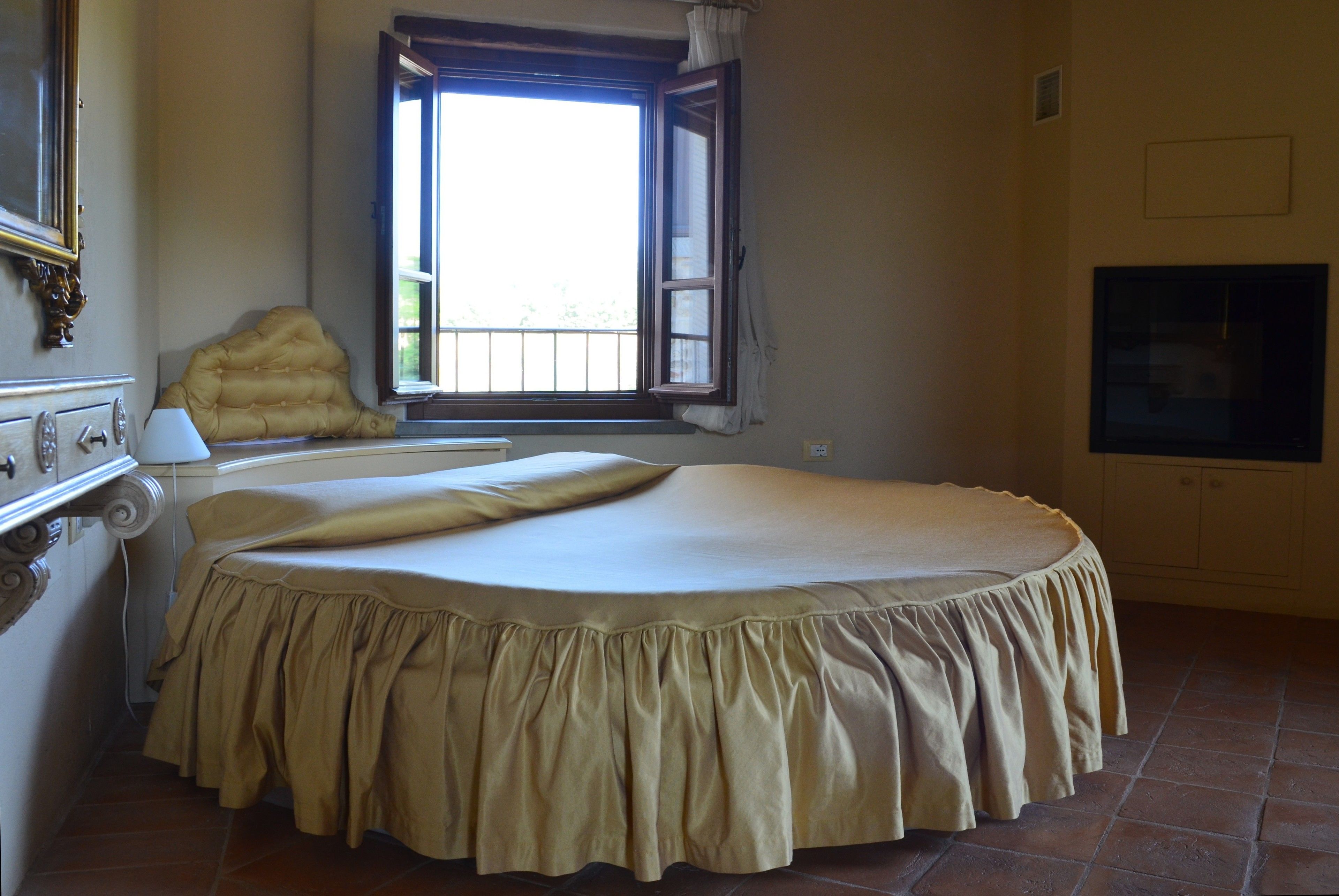 Quarto com cama grande, janela com cortinas, televisão e cômoda.