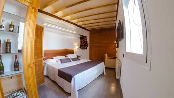 Quarto com cama, vigas de madeira, parede de tijolo, estante com garrafas e uma janela.