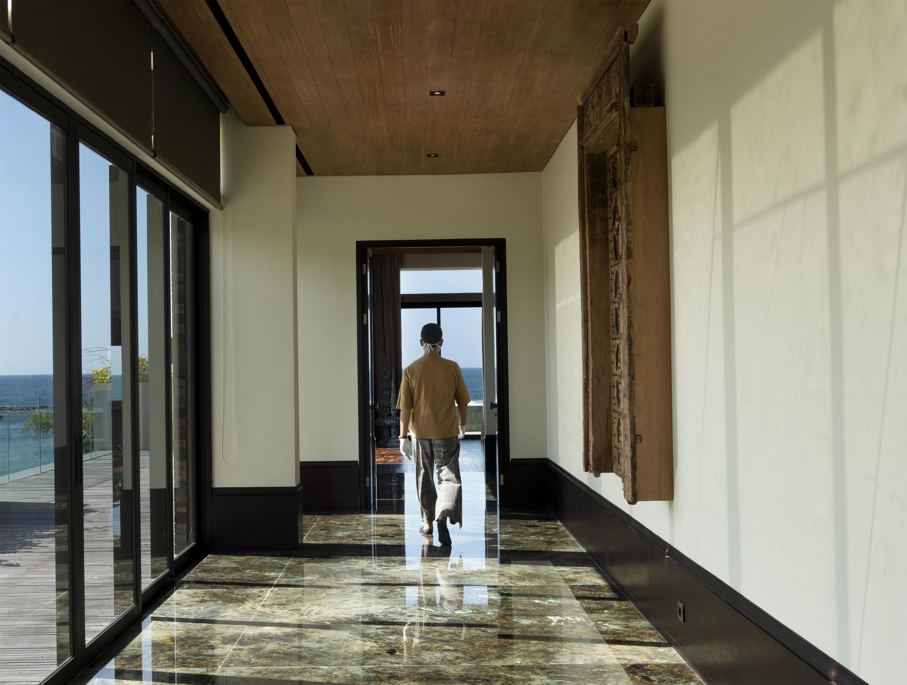 Um corredor com teto de madeira, grandes portas de vidro que dão para uma varanda e piso de mármore.