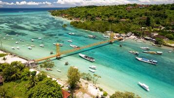 Uma área costeira com uma ponte ligando dois trechos de terra, águas turquesa cristalinas e vários barcos.