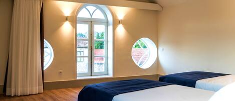 Quarto com duas camas, uma grande janela em arco e duas luzes fixadas na parede.