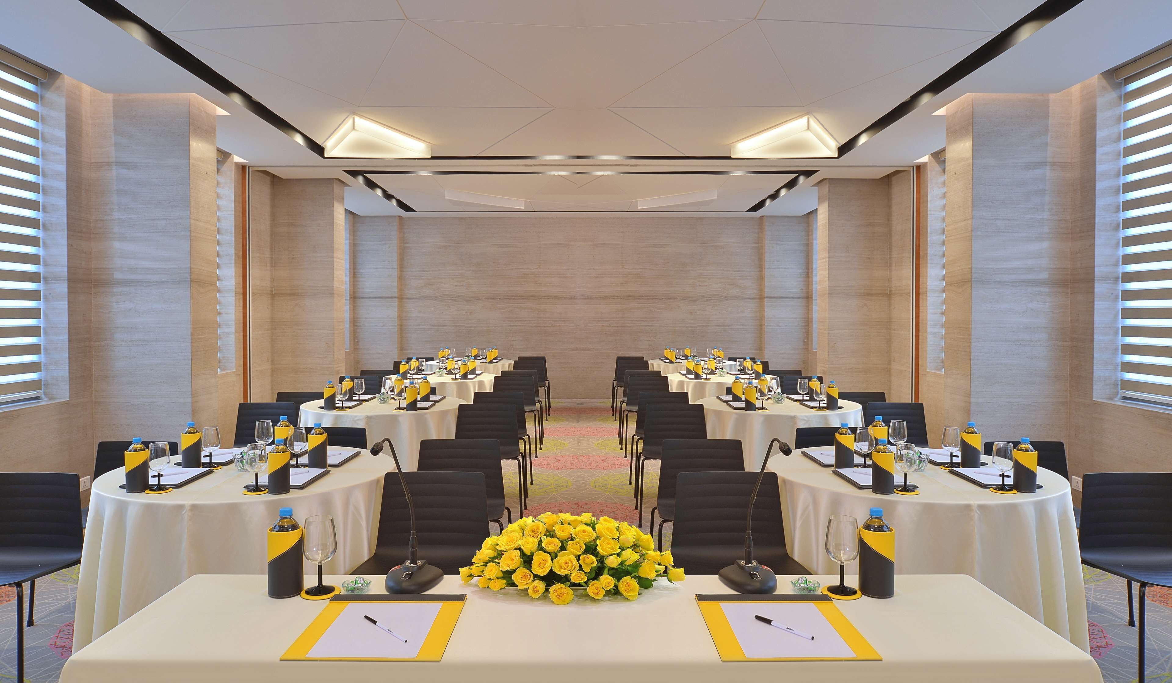 Sala de conferência com várias mesas, cadeiras e um arranjo floral central.