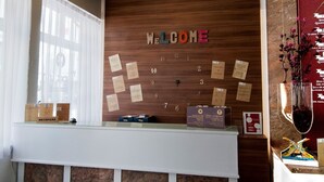 Uma receção com um letreiro 'WELCOME', um candelabro, um mural com notas e um vaso com flores.