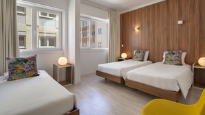 Quarto de hotel com duas camas, uma parede de destaque em madeira, vista para edifícios e uma cadeira amarela.