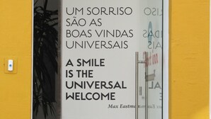 Uma porta com uma citação motivacional em português, um painel de vidro e uma planta ao fundo.