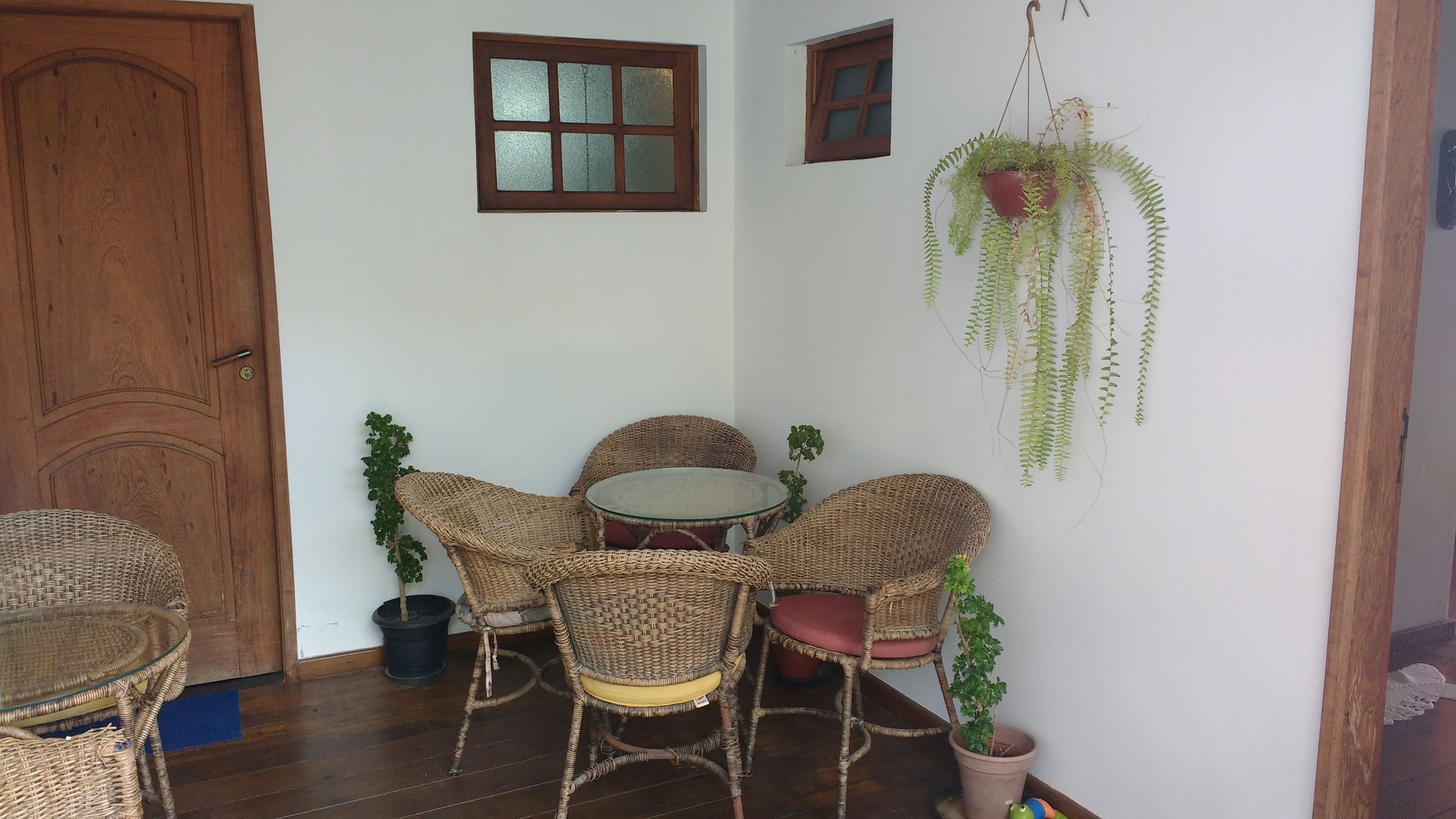 Quarto com mobiliário de vime, uma mesa redonda de vidro e plantas em vasos.