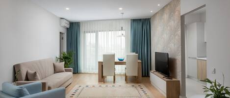 Uma sala de estar moderna com um sofá, uma mesa de centro, uma televisão e uma área de jantar com cadeiras e uma mesa.