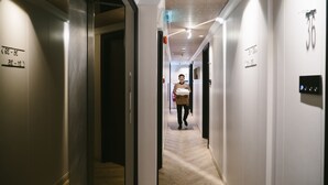 Corredor moderno de hotel com uma pessoa caminhando, iluminado por luzes embutidas no teto e portas numeradas.