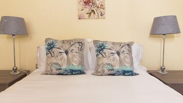 Cama com duas almofadas decorativas com desenhos de borboletas, com duas luminárias de cada lado.