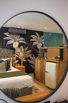 Quarto com cama, mesa de cabeceira, luminária, guarda-roupa e um pequeno frigorífico.