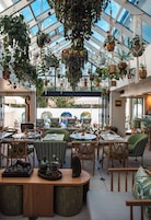 Espaço interior com plantas pendentes, áreas de estar e vista através de teto de vidro.