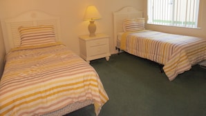 Quarto com duas camas, mesa de cabeceira, abajur, relógio e janela com cortinas.