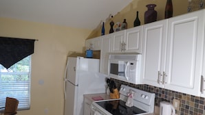 Uma cozinha compacta com armários brancos, geladeira, forno, micro-ondas e chaleira.