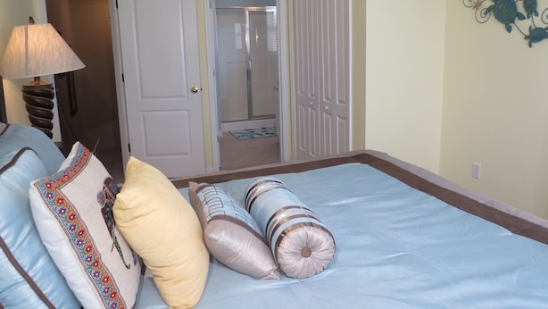 Quarto com cama, travesseiros, luminária, armário e chuveiro.