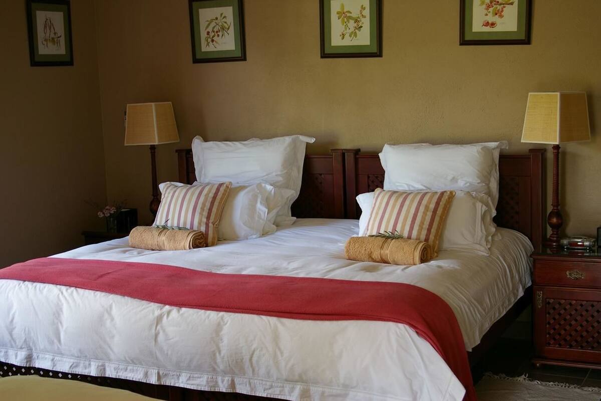 Uma cama de casal com roupa de cama branca e almofadas listradas, duas mesas de cabeceira com luminárias e arte floral na parede.