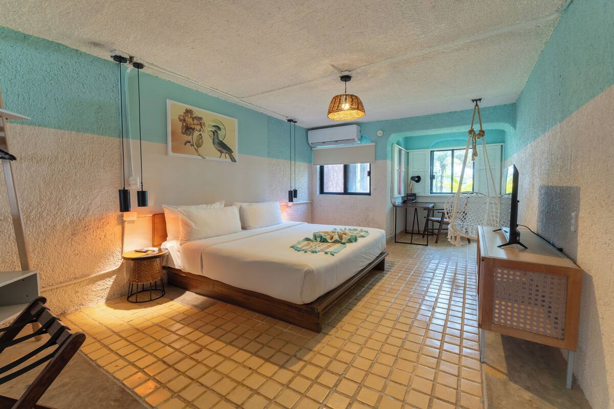 Quarto com cama, mesa de cabeceira, luminária e vista para o exterior.