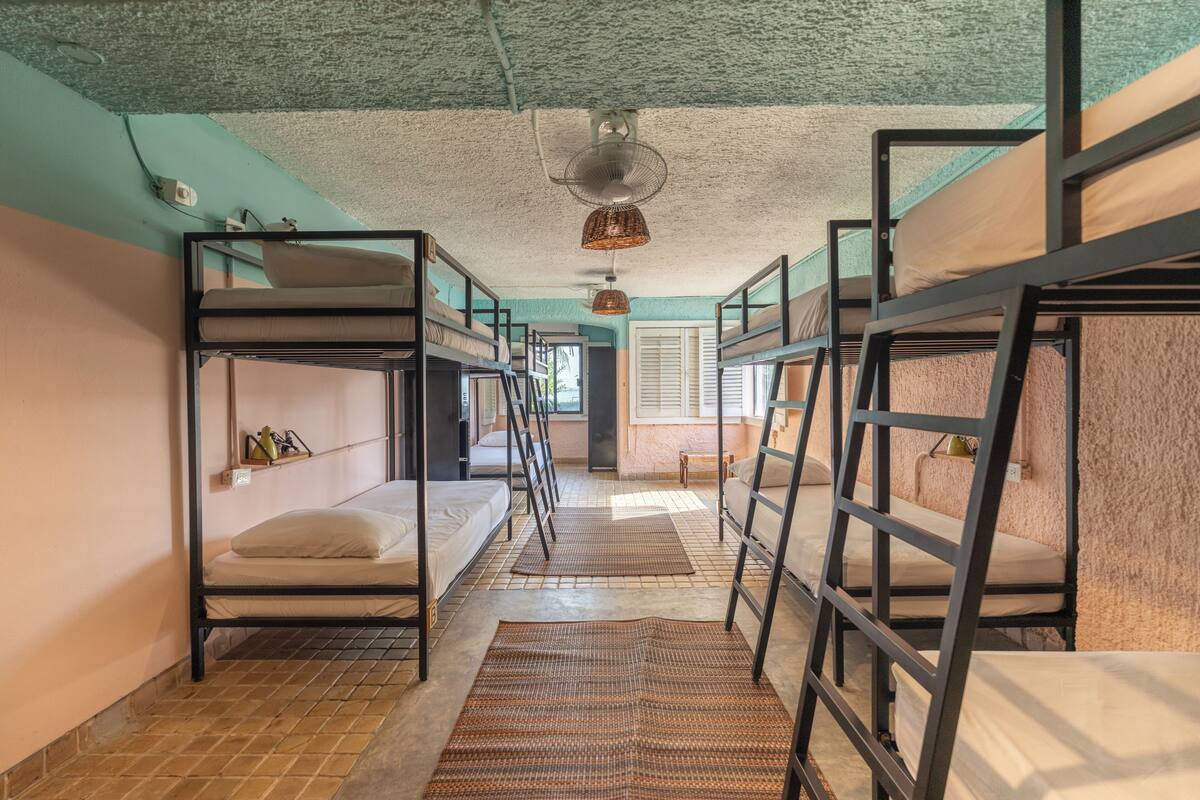 Quarto de dormitório com beliches, um ventilador e um tapete estampado.