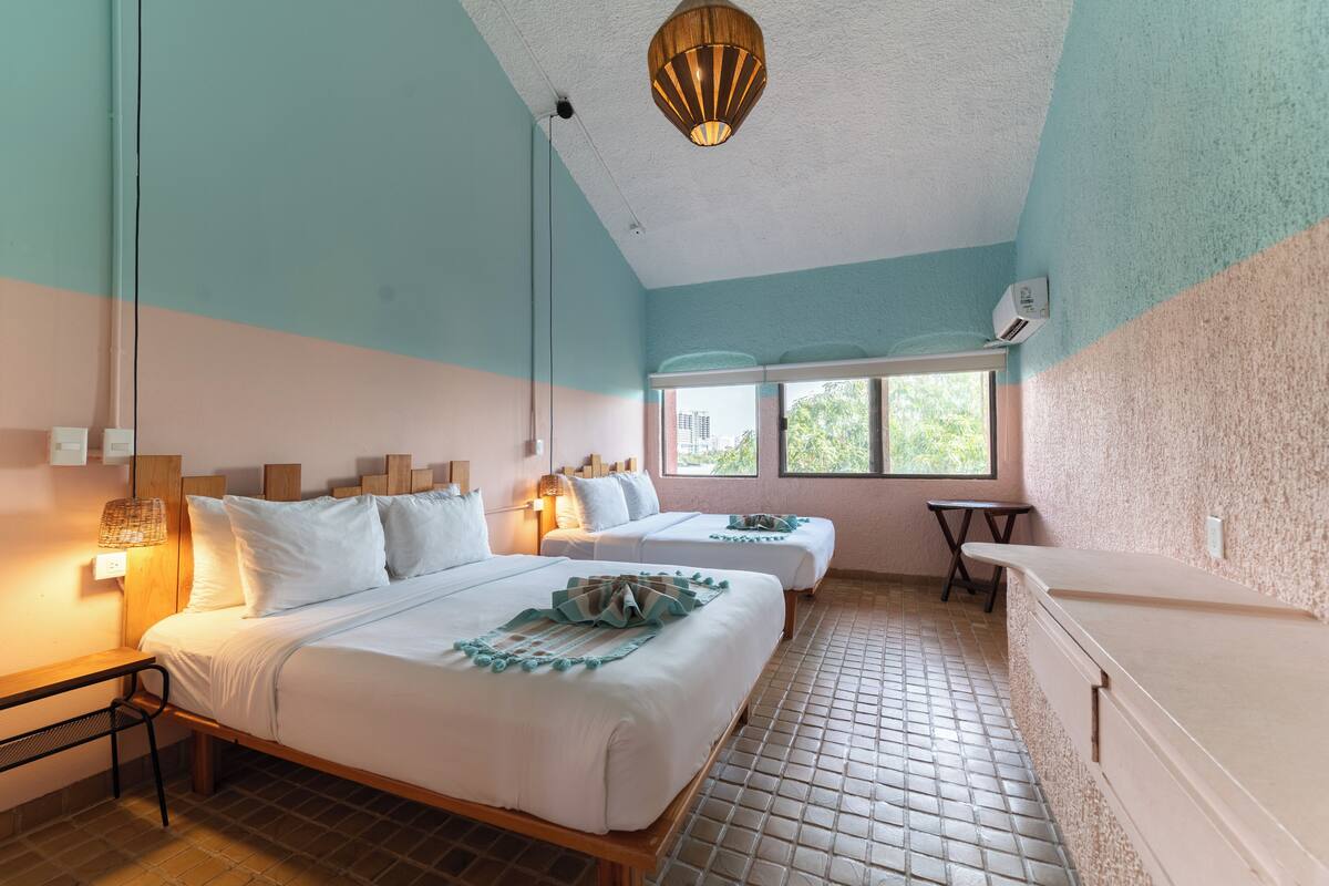 Quarto com duas camas, uma escrivaninha, uma cadeira, uma janela e ar condicionado.