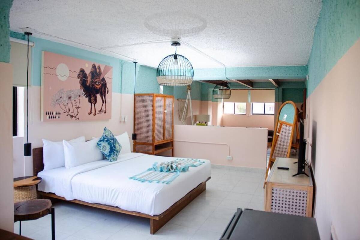 Quarto com cama, espelho, luminária pendente e pintura na parede.